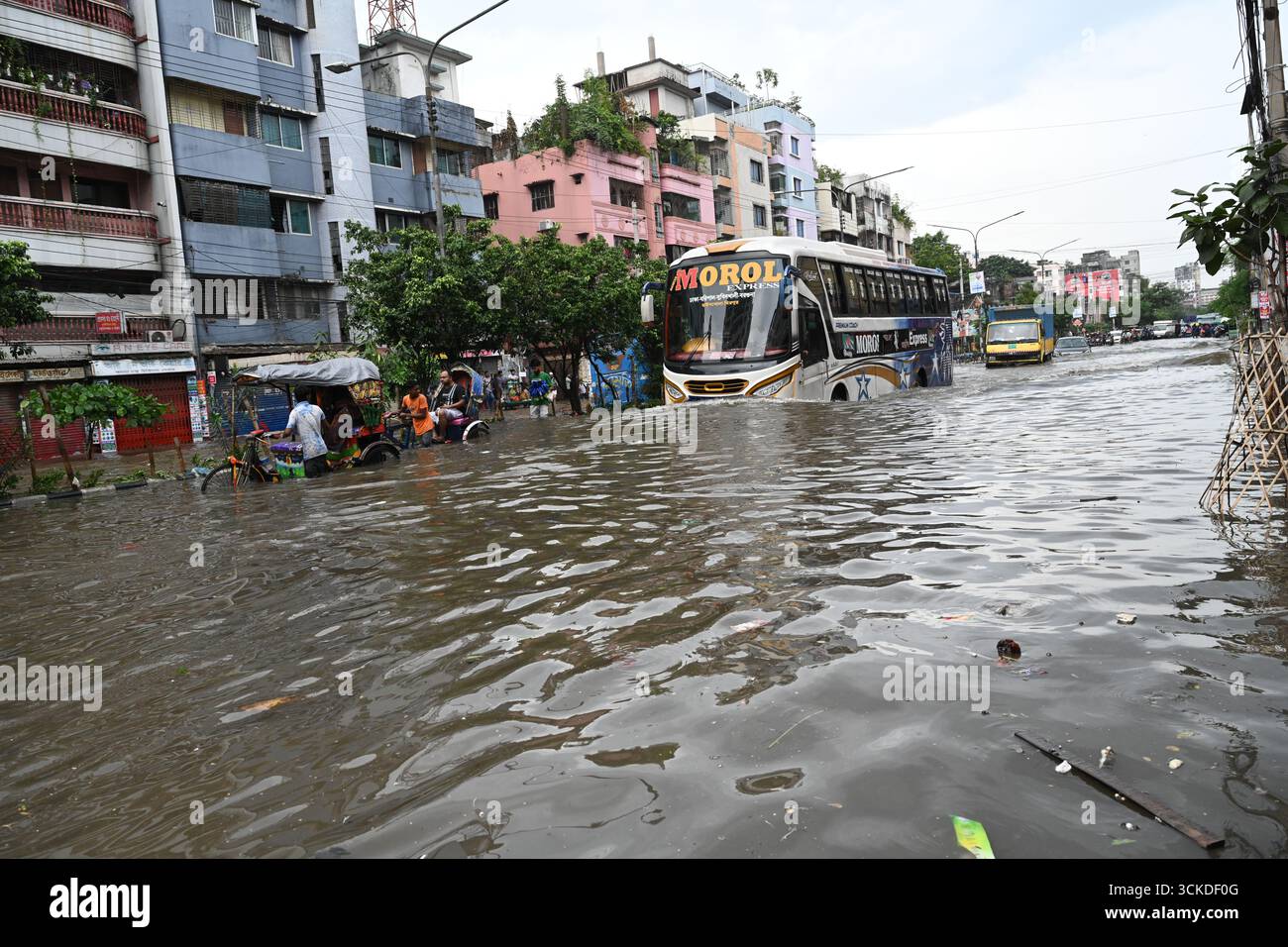 Vehicles and rickshaws drive with passengers through the waterlogged streets of Dhaka ...