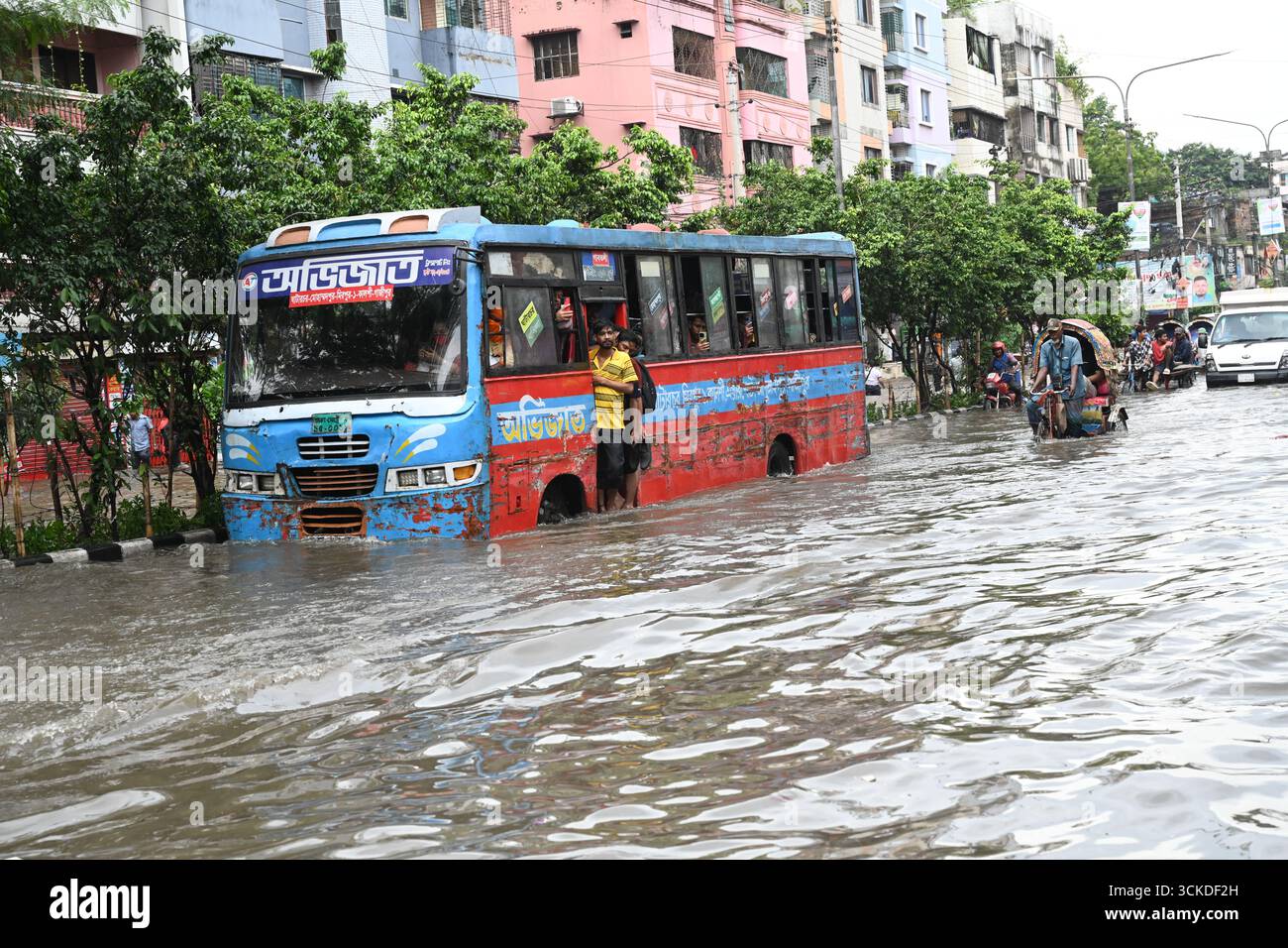 Vehicles and rickshaws drive with passengers through the waterlogged streets of Dhaka ...
