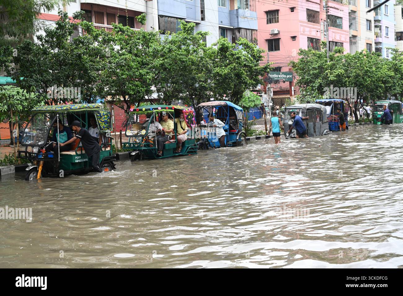 Vehicles and rickshaws drive with passengers through the waterlogged streets of Dhaka ...