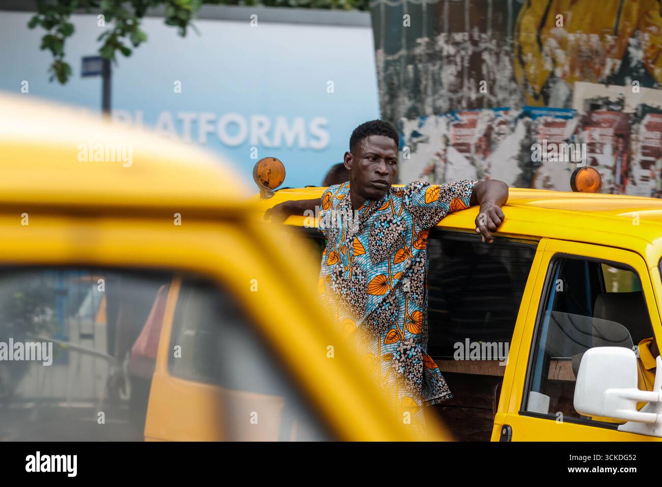 A bus conductor hangs onto a moving yellow danfo bus, a vibrant symbol ...