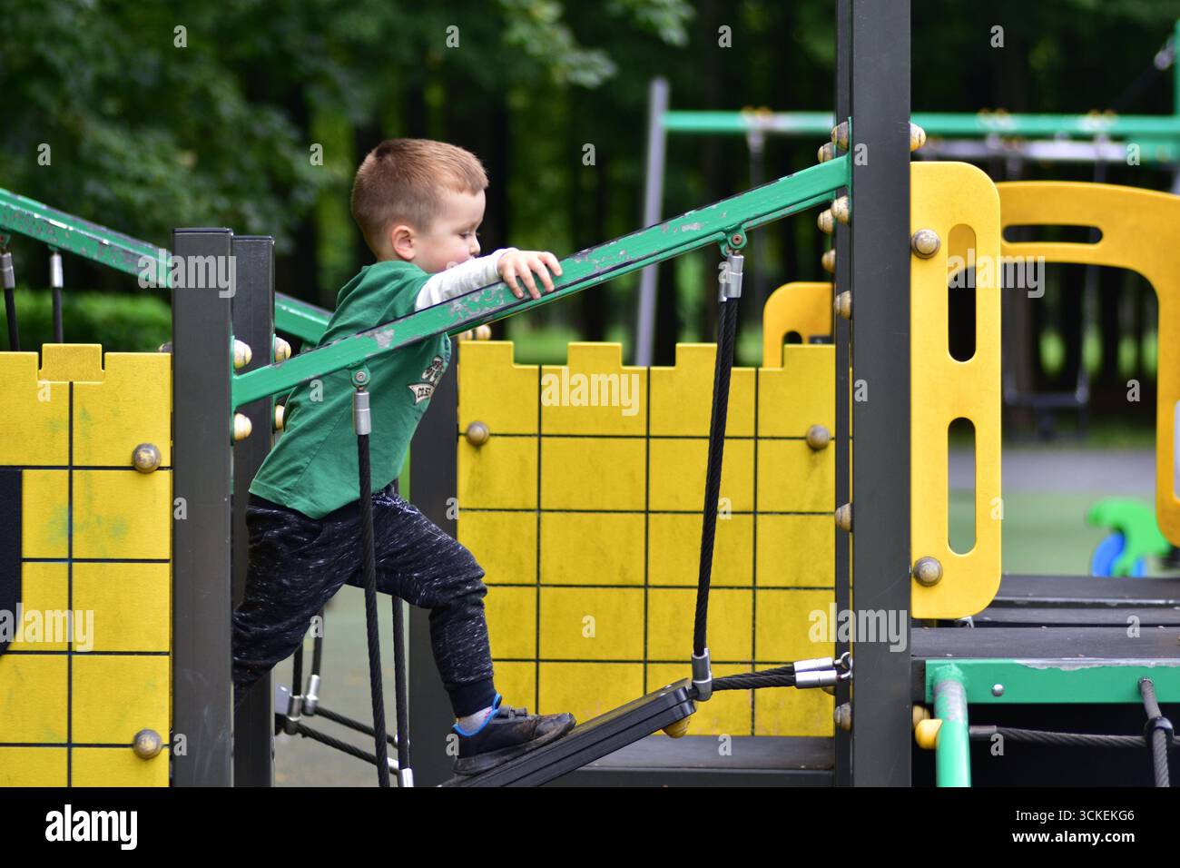 Boy in green shirt carefully crossing suspension bridge at playground ...