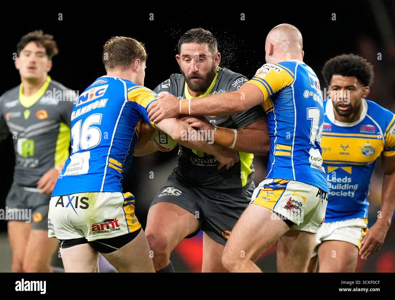 Catalans Dragons' Julian Bousquet (centre) is tackled by Leeds Rhinos ...