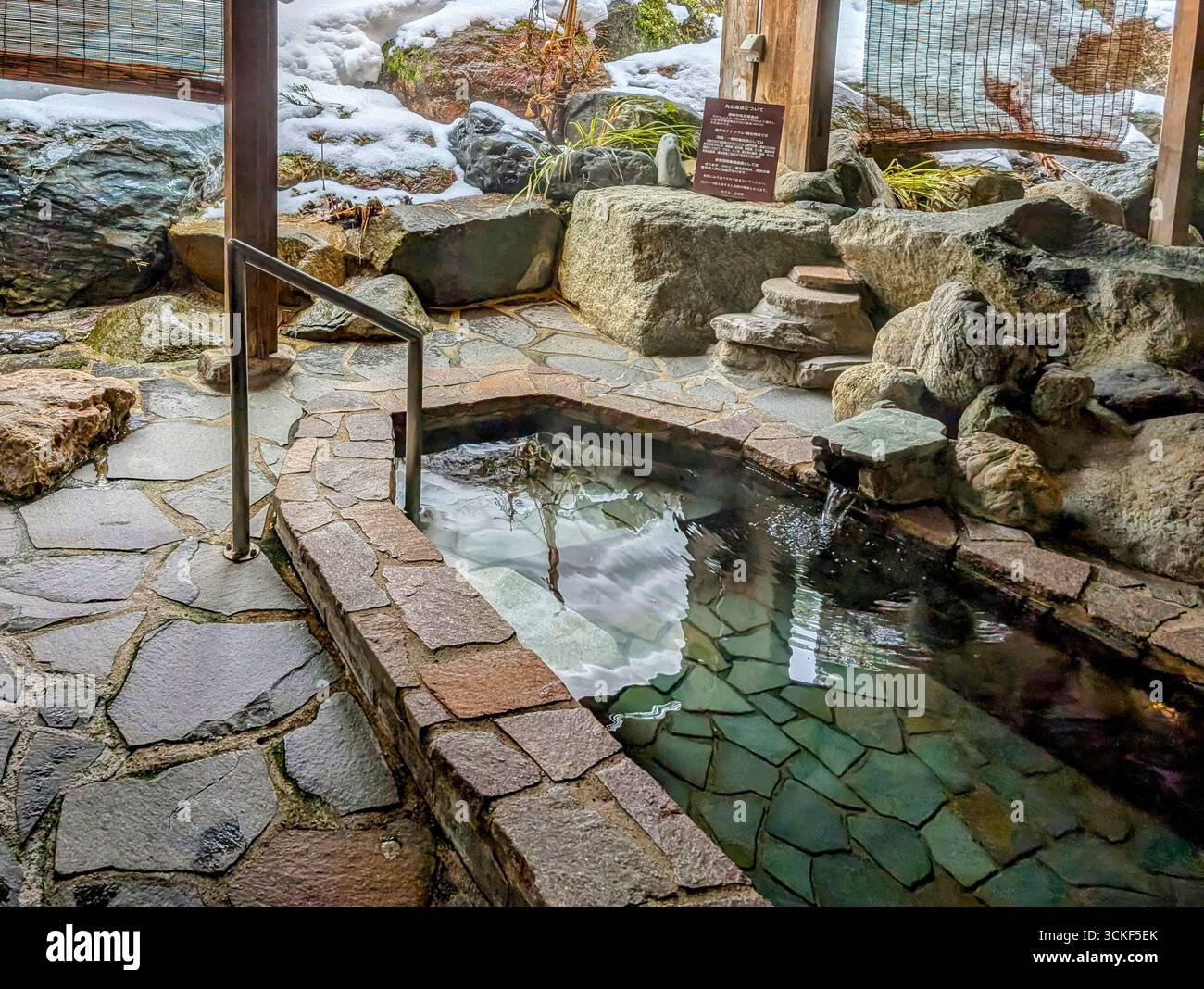 Steaming water in traditional stone onsen bath surrounded by snow in ...