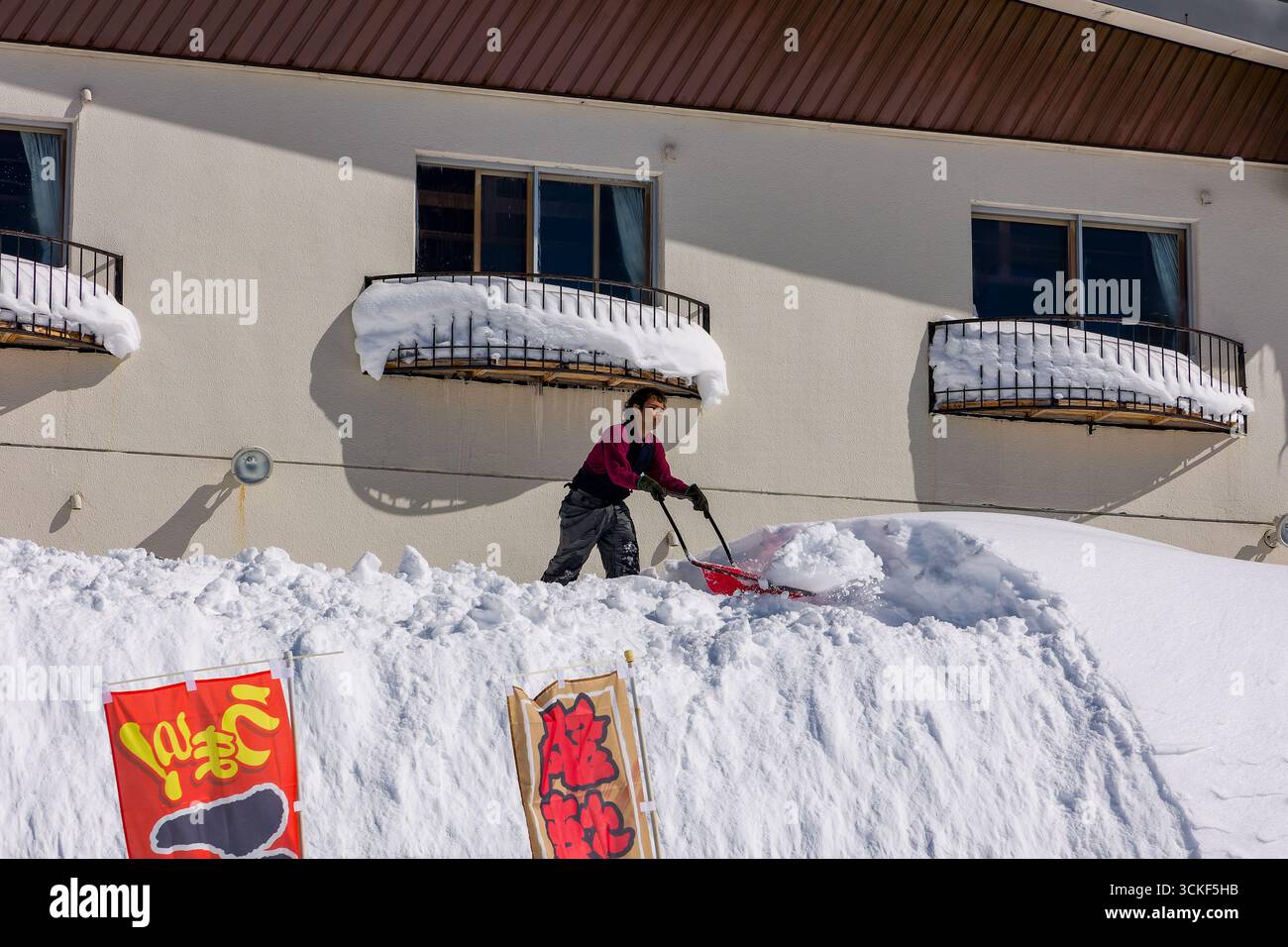 Man clearing extremely deep snow with a red shovel from a building in ...