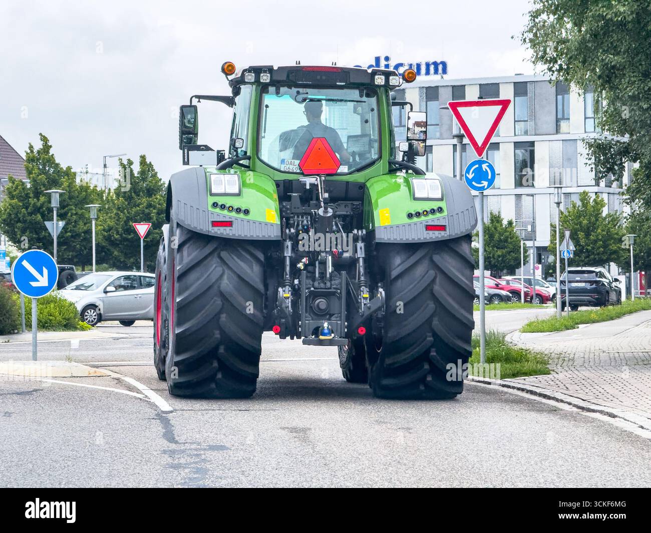 Green modern Fendt tractor navigating an urban road near trees and a ...