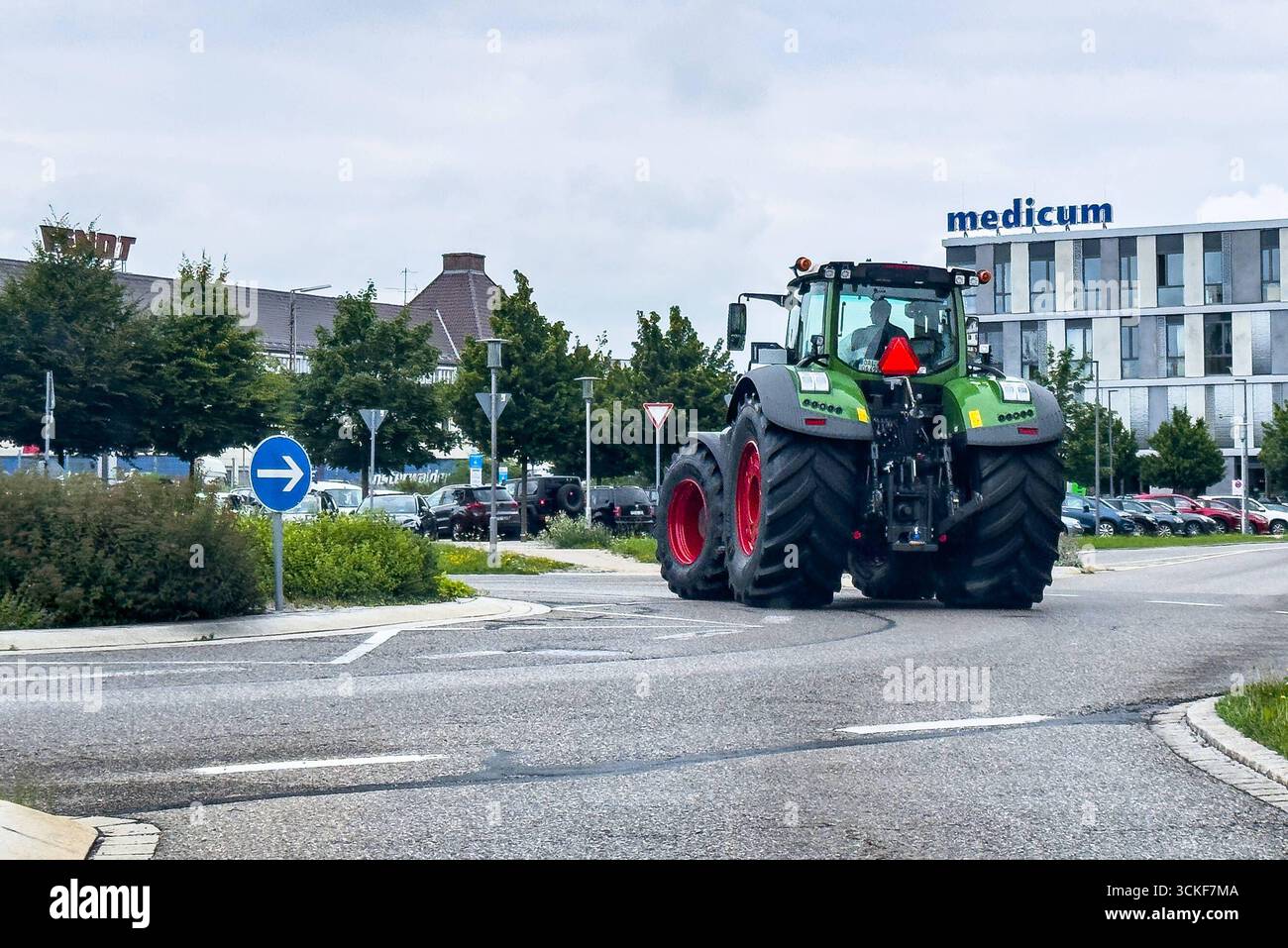 Green modern Fendt tractor navigating an urban road near trees and a ...