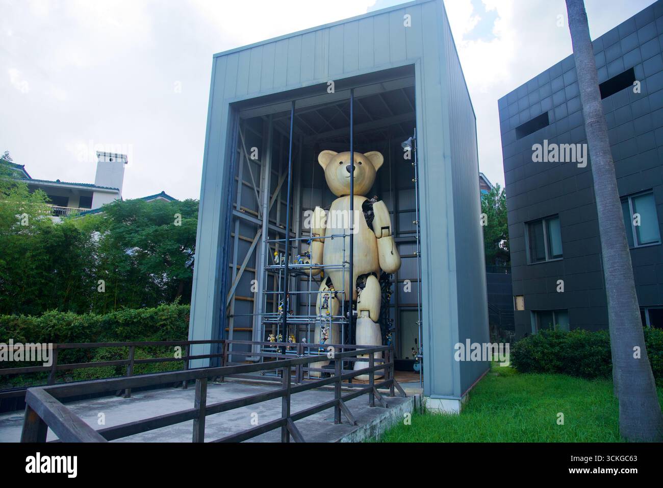 A colossal teddy bear figure stands in a tall outdoor shed‑like frame ...
