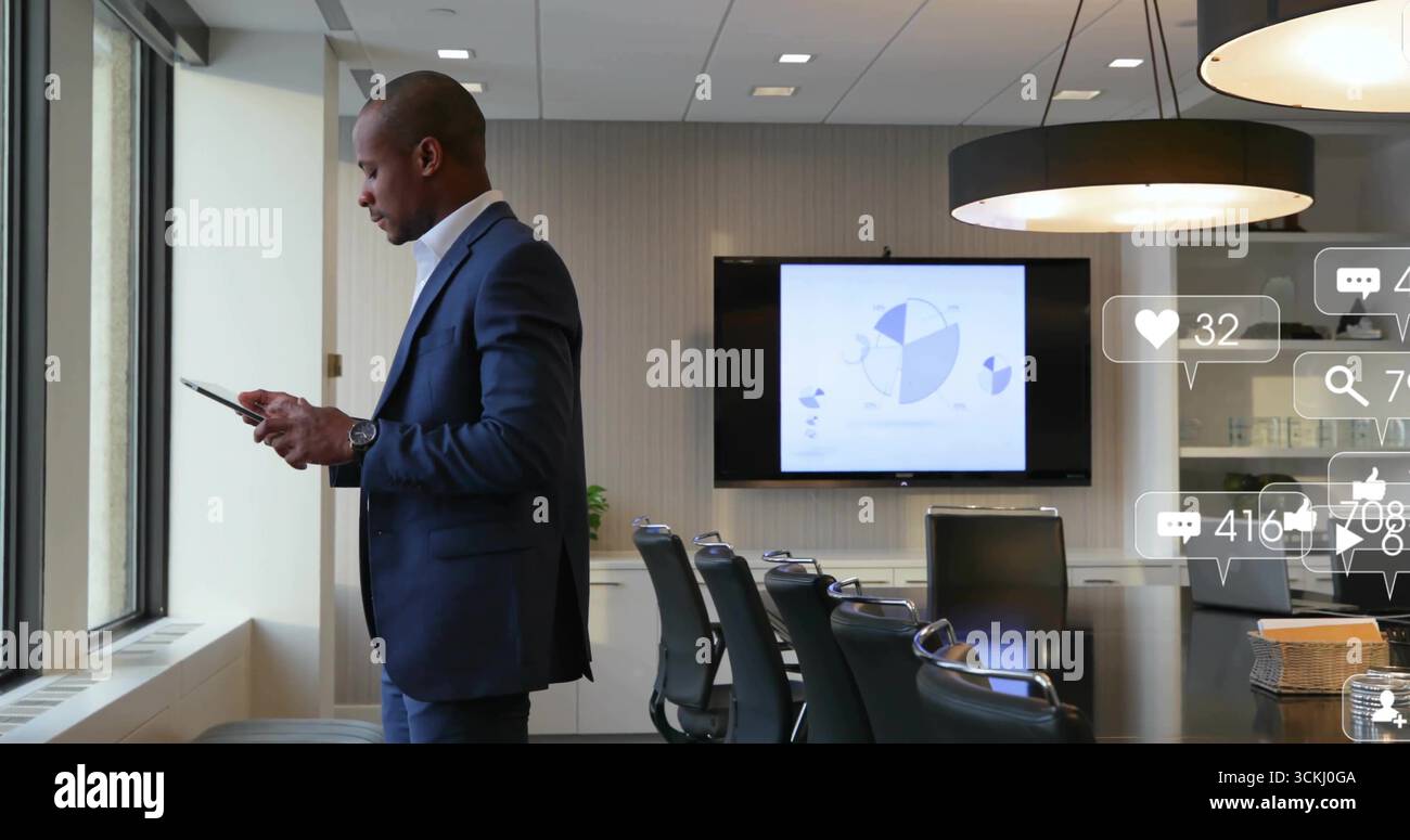Standing executive by window wearing navy suit holding digital tablet ...