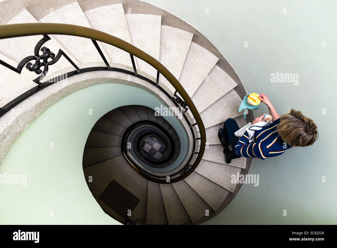 Woman walking up a swirling staircase i Audergem, Brussels, Belgium ...