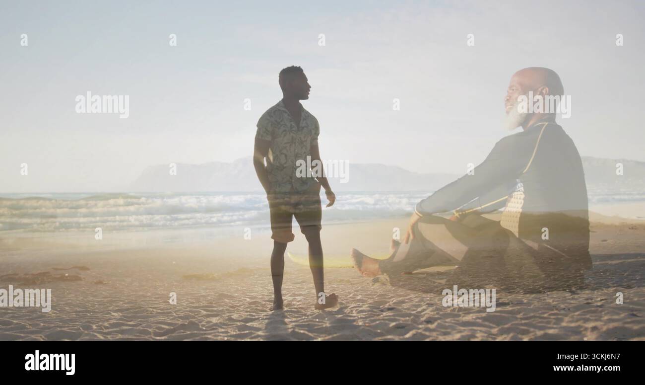 Standing man gazing at horizon on sandy shore, with meditating father ...