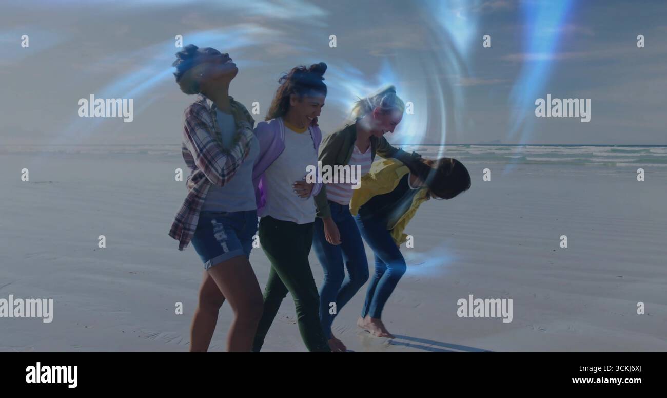 Walking group of four women linking arms and laughing on wet sandy ...