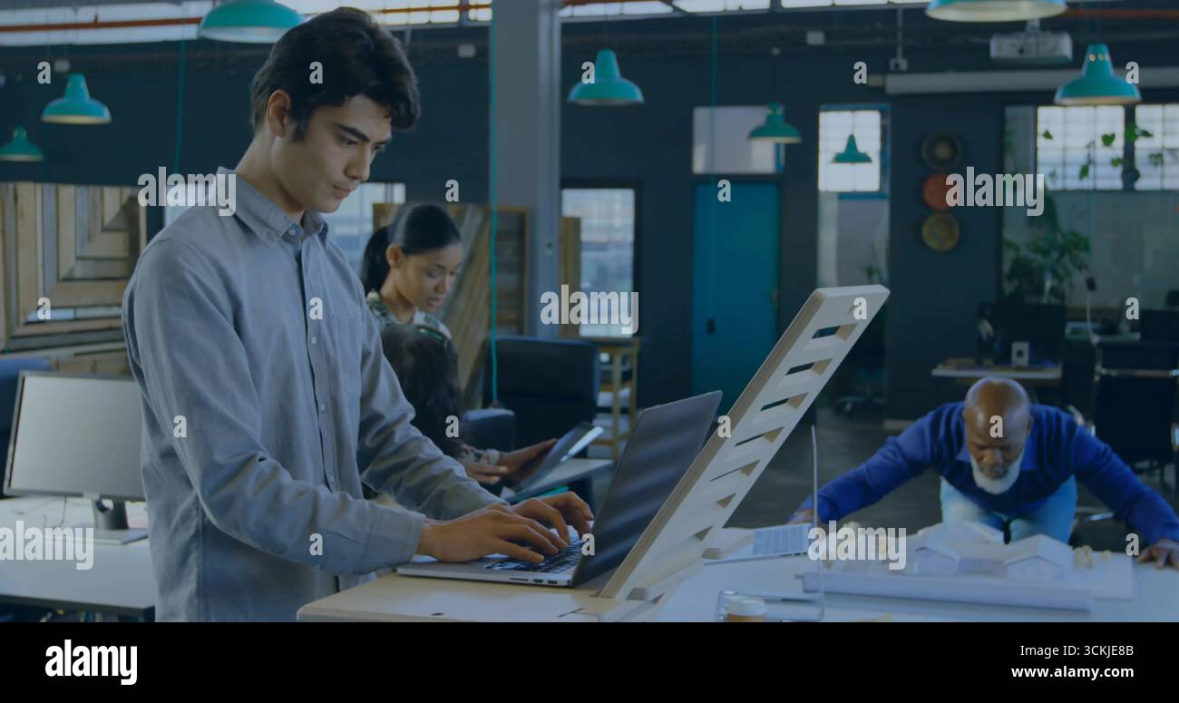 Typing standing designer on laptop stand in open-plan design studio ...