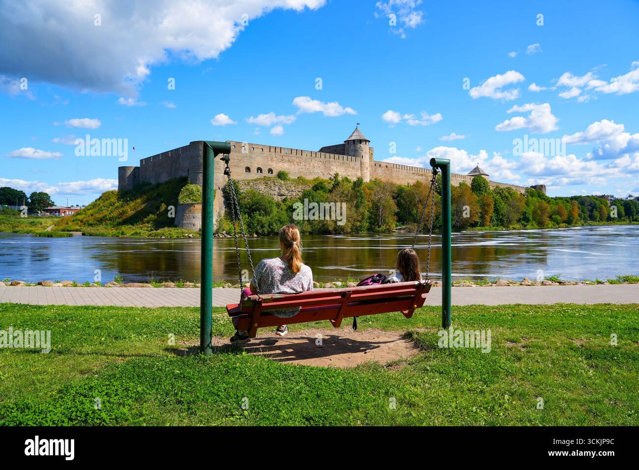 Blonde woman sitting with her daughter on a bench facing the Ivangorod ...