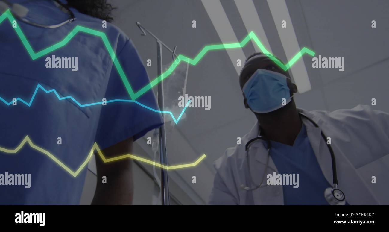 Two healthcare workers reviewing vital sign graphs in hospital room ...