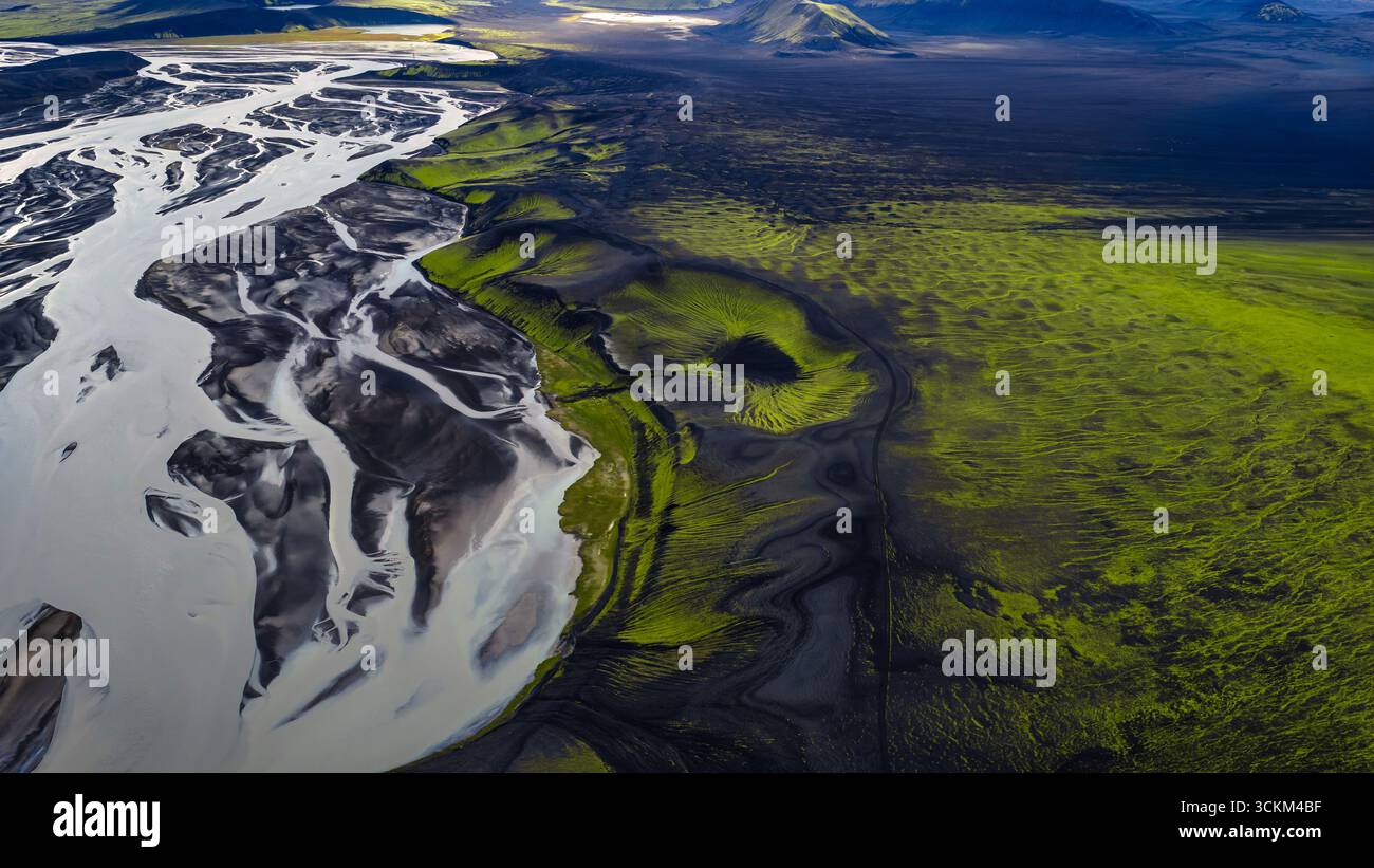 Braided river with silty water flows through dark volcanic terrain ...