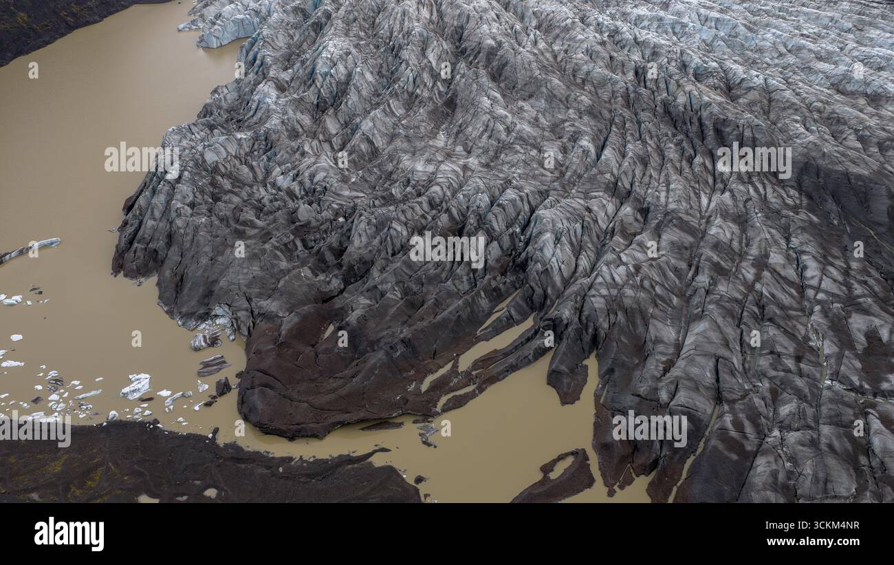 A glacier with crevassed surface descends into a milky brown glacial ...