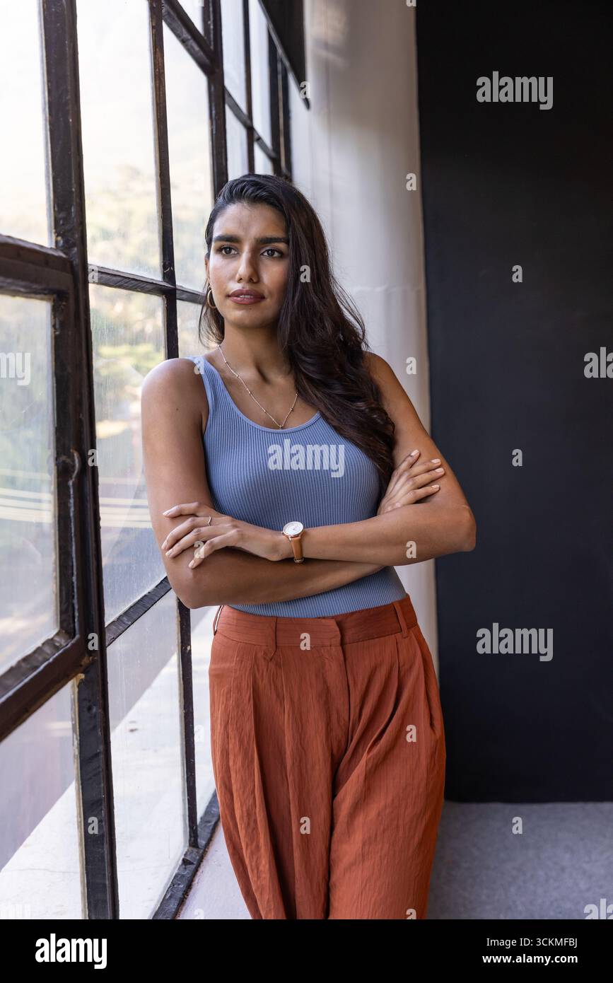 Indian woman in her 30s standing by metal-framed window in studio ...
