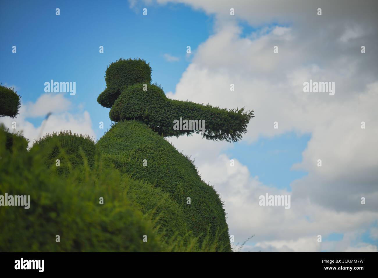 Unique topiary sculpture resembling a figure in a garden under a blue ...