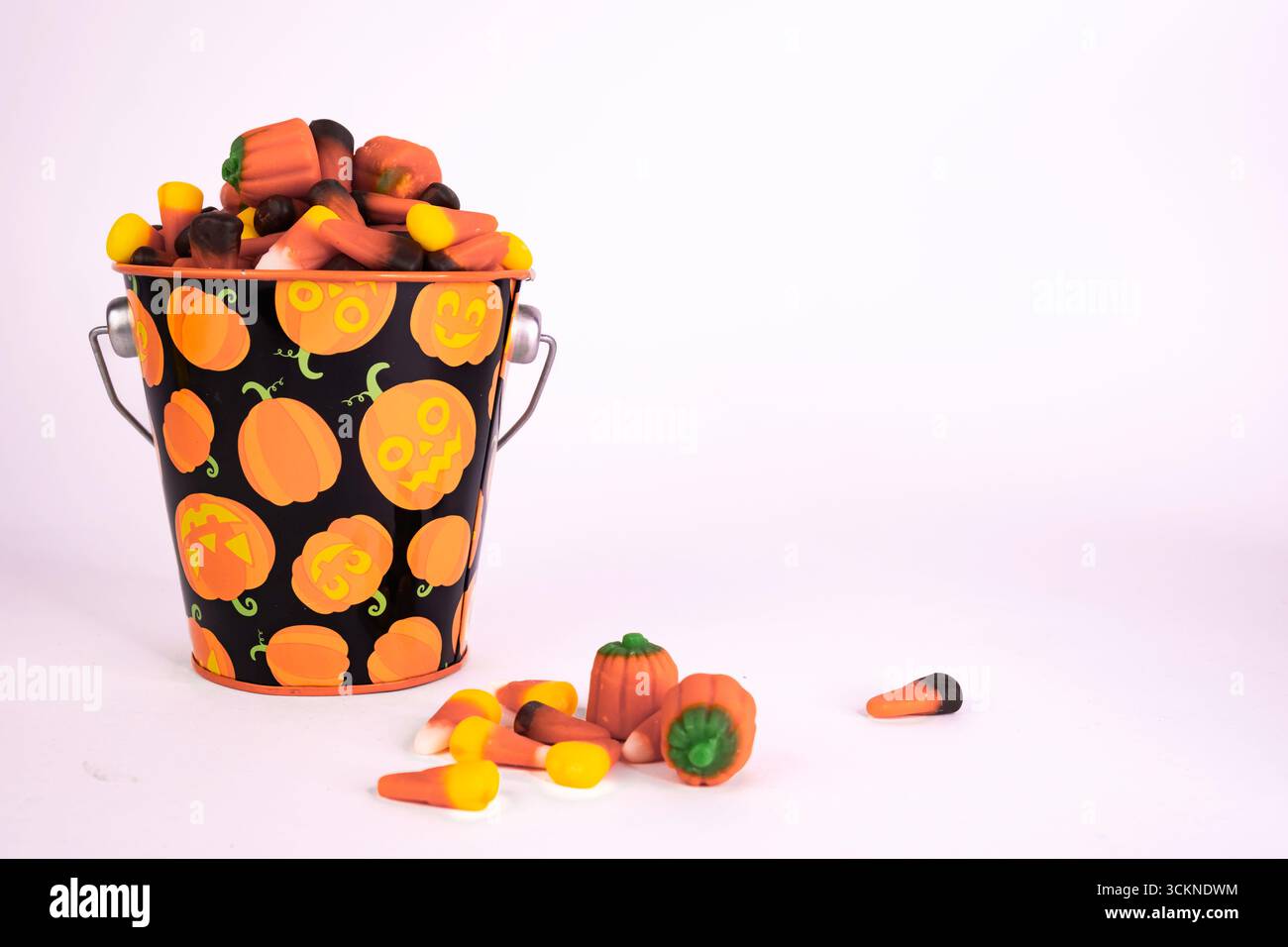 A bucket of Halloween candy overflowing onto the surface. Candy corn ...