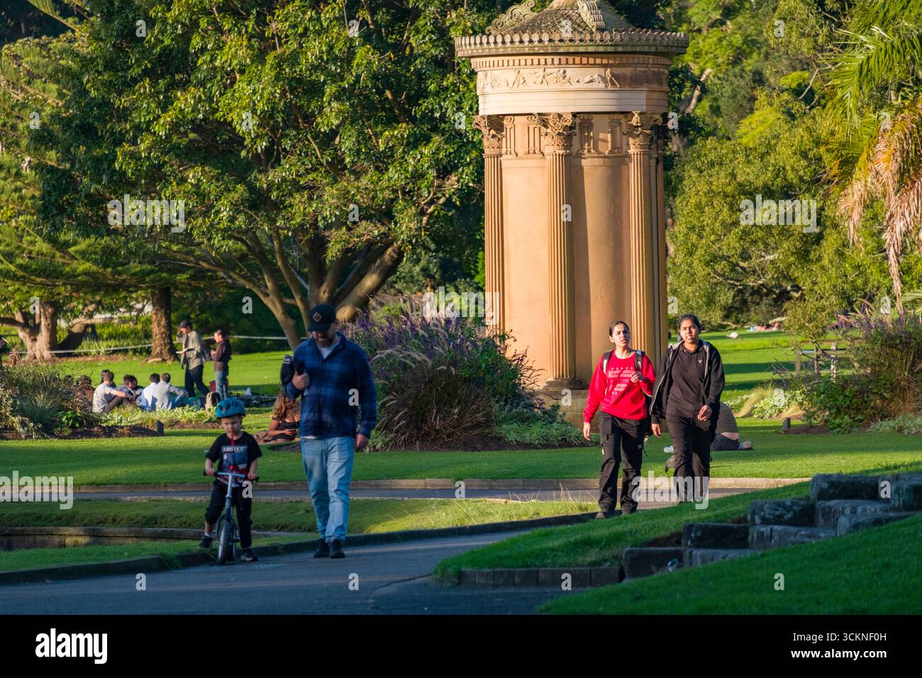 Groups of people walk and relax in a park with lush greenery and ...