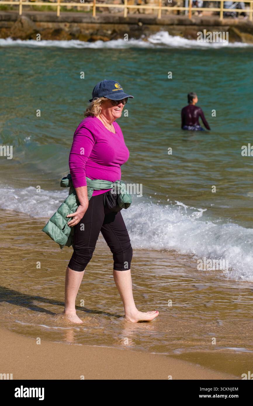 A woman enjoys a leisurely walk along a sandy beach, barefoot by the ...