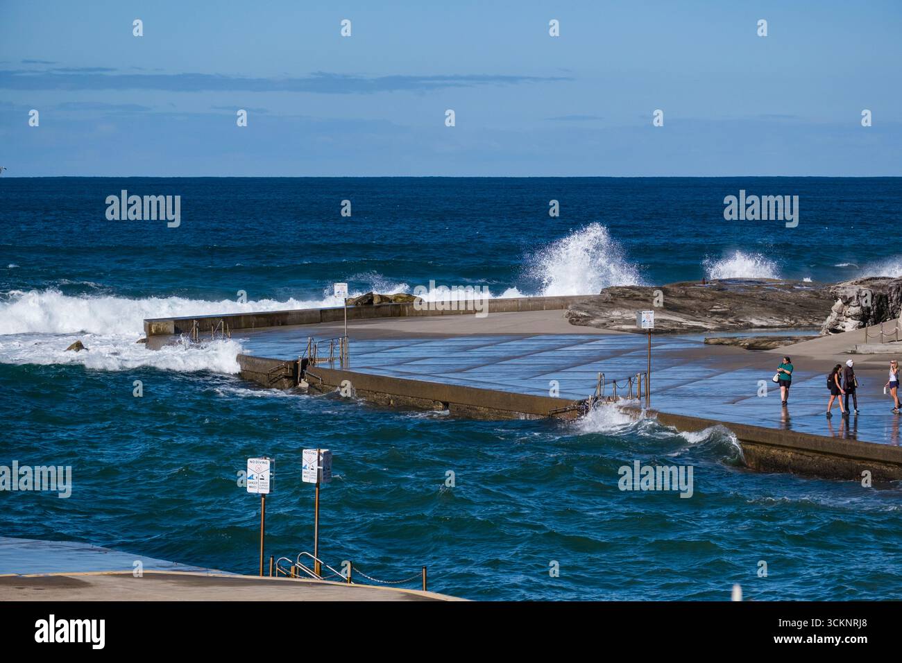 A seaside ocean pool with waves splashing on its perimeter, as ...