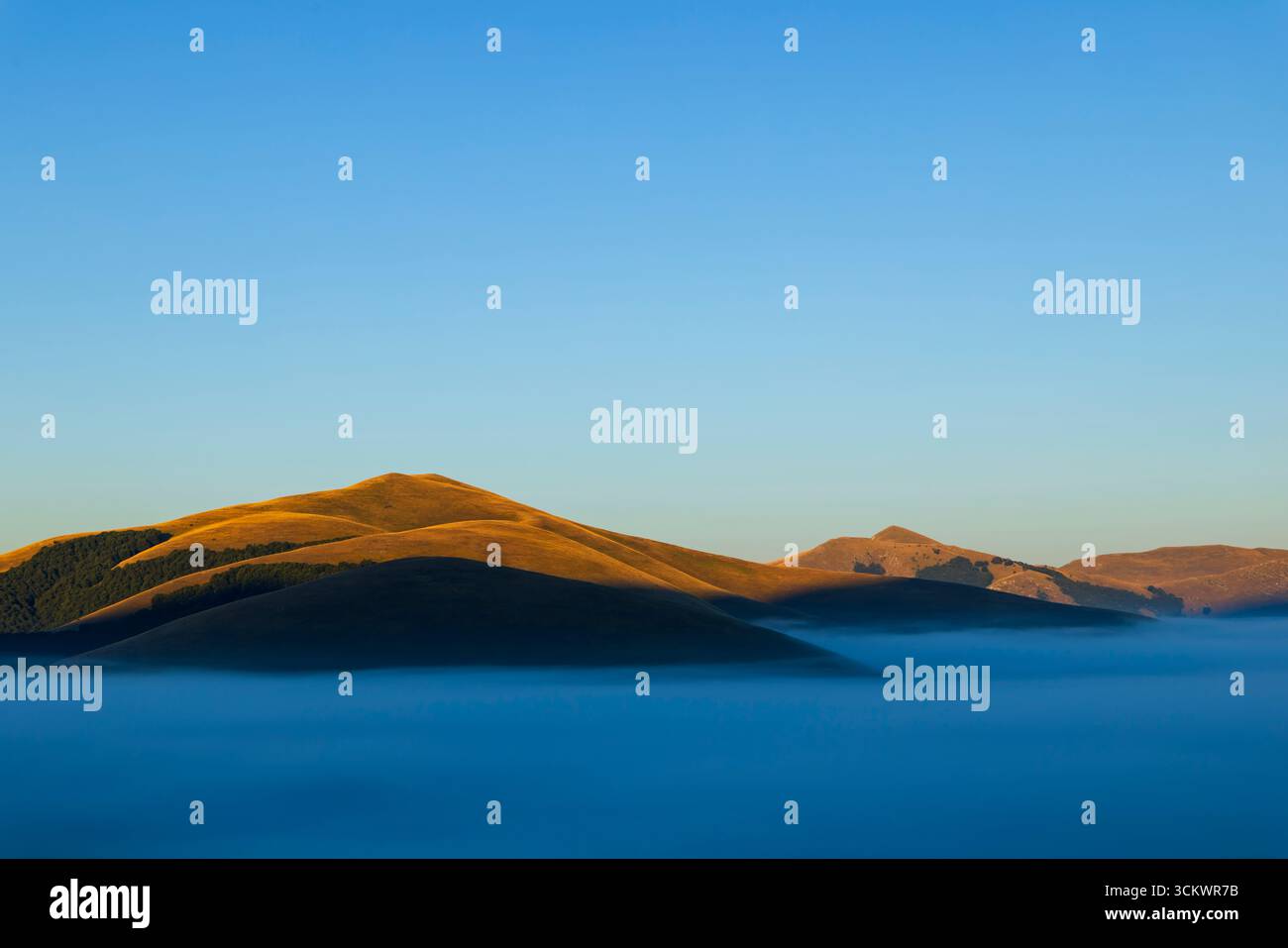 Warm light of sunrise illuminating the top of the hills emerging from ...