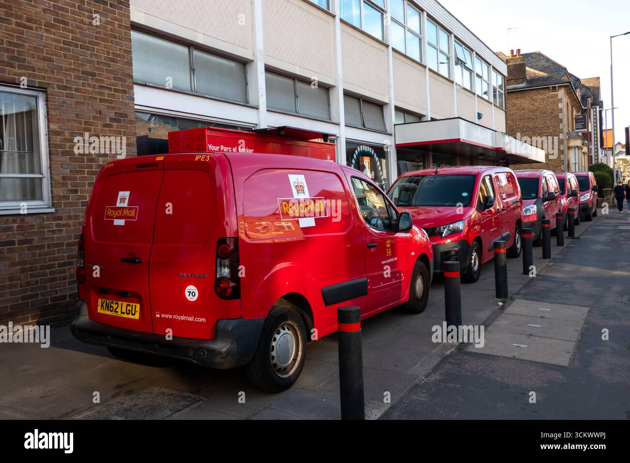 A row of red Royal Mail delivery vans are parked in front of the ...