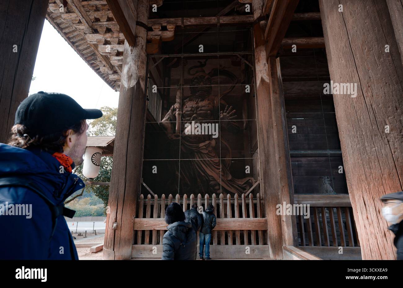 Visitors pass by the fierce guardian statue inside the wooden gate of ...