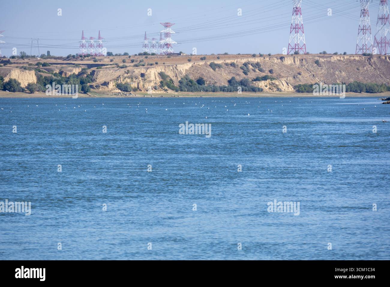 Scenic view of a wide river flowing with tall electricity pylons and ...