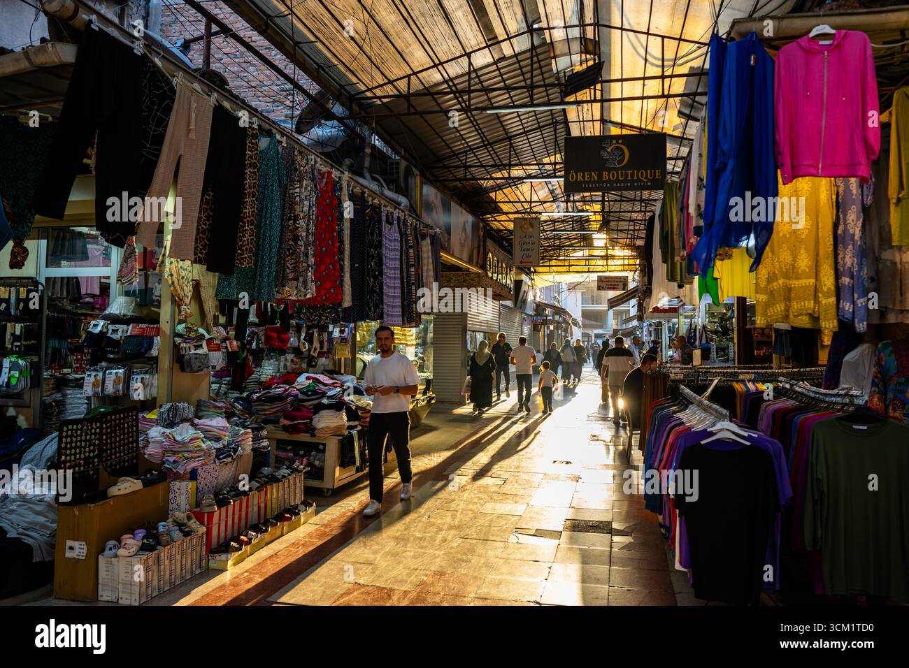 People walk through a covered bazaar with clothing shops, fabric stalls ...