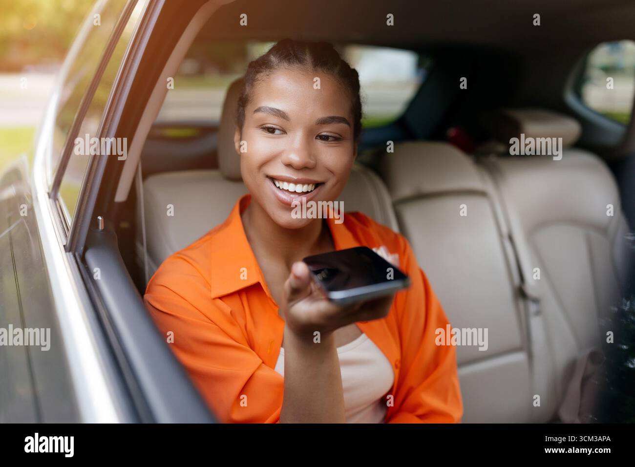 Smiling black woman using smartphone in car back seat, recording voice ...
