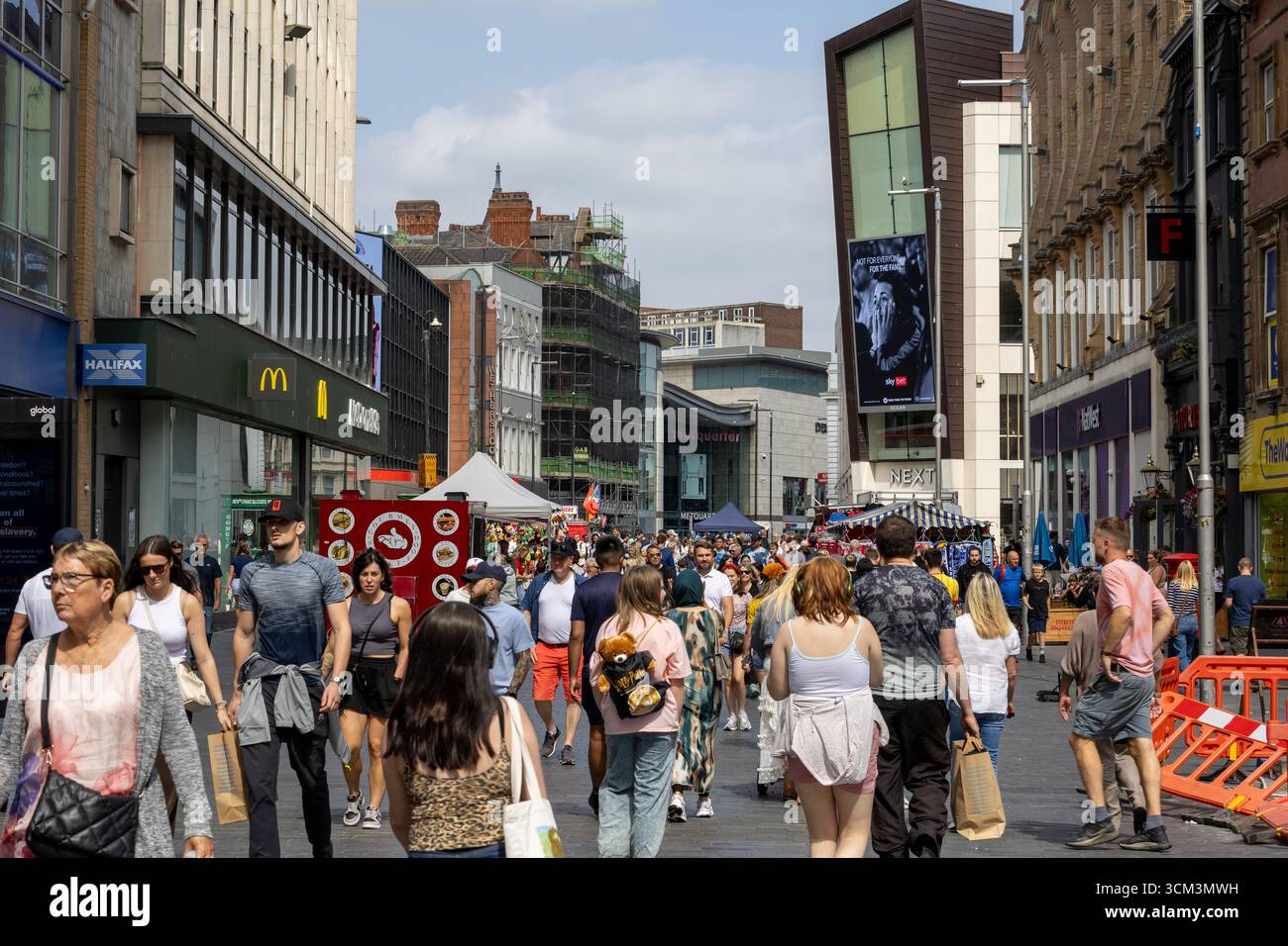 A busy street scene with pedestrians walking past shops, stalls, and ...