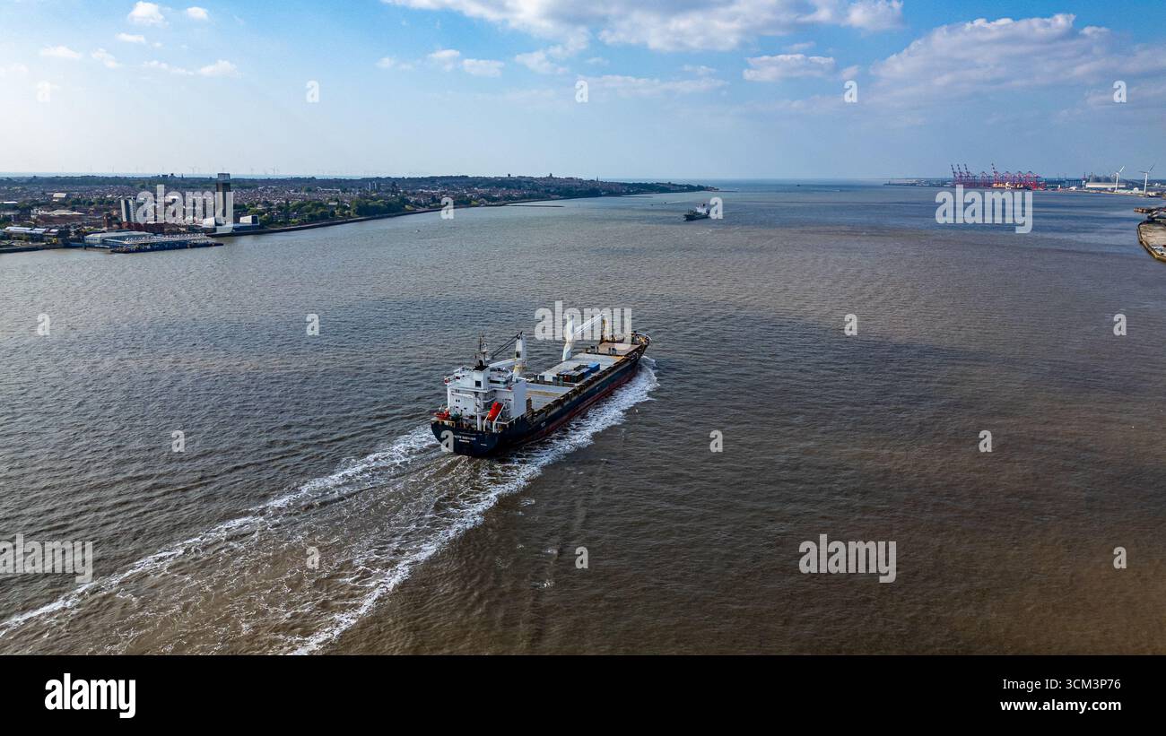 An aerial view shows a cargo ship sailing on a wide river, with a city ...