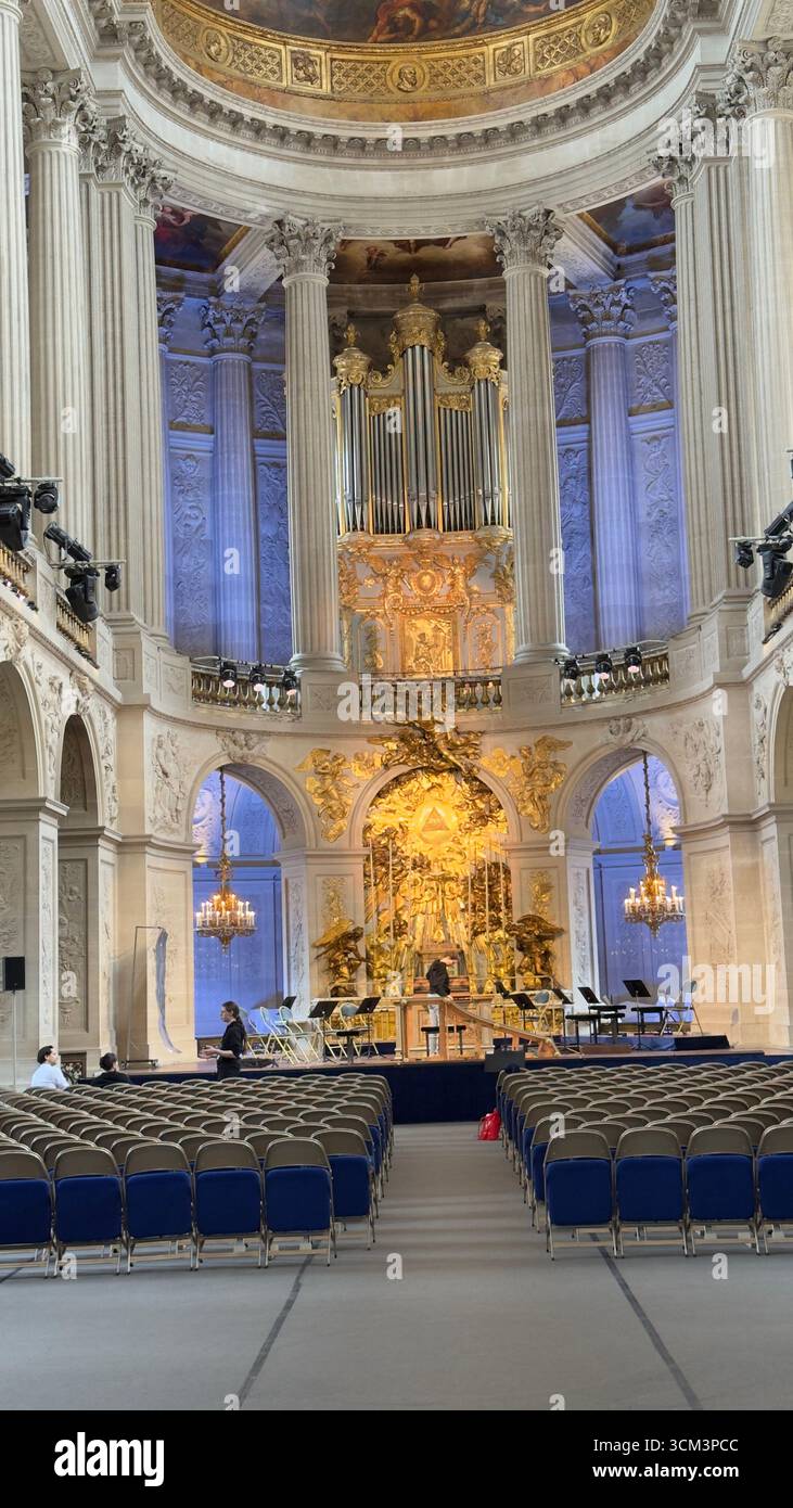 A grand hall features rows of blue chairs facing a stage with an ornate ...