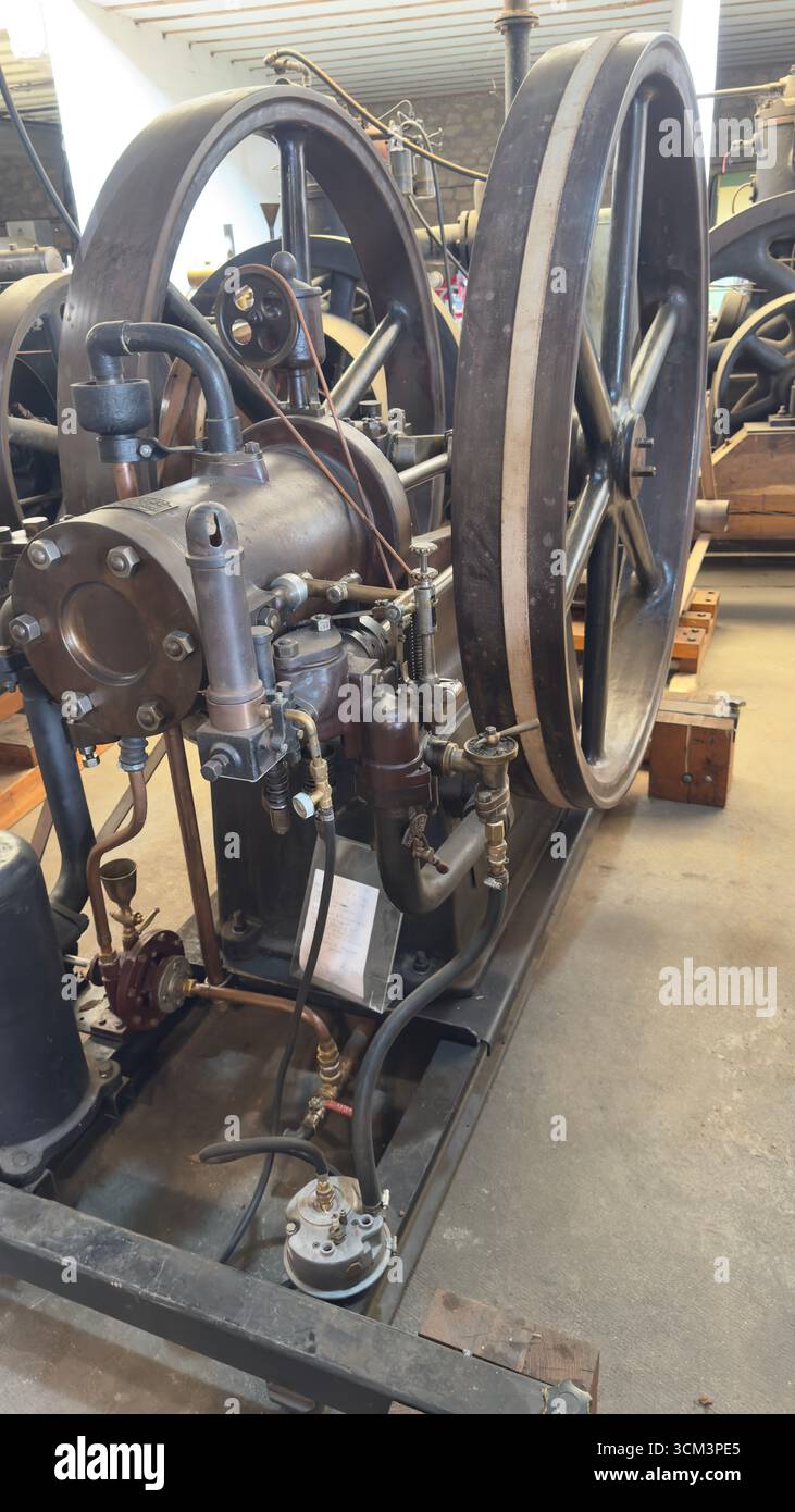 An antique engine features large flywheels, copper piping, and a ...