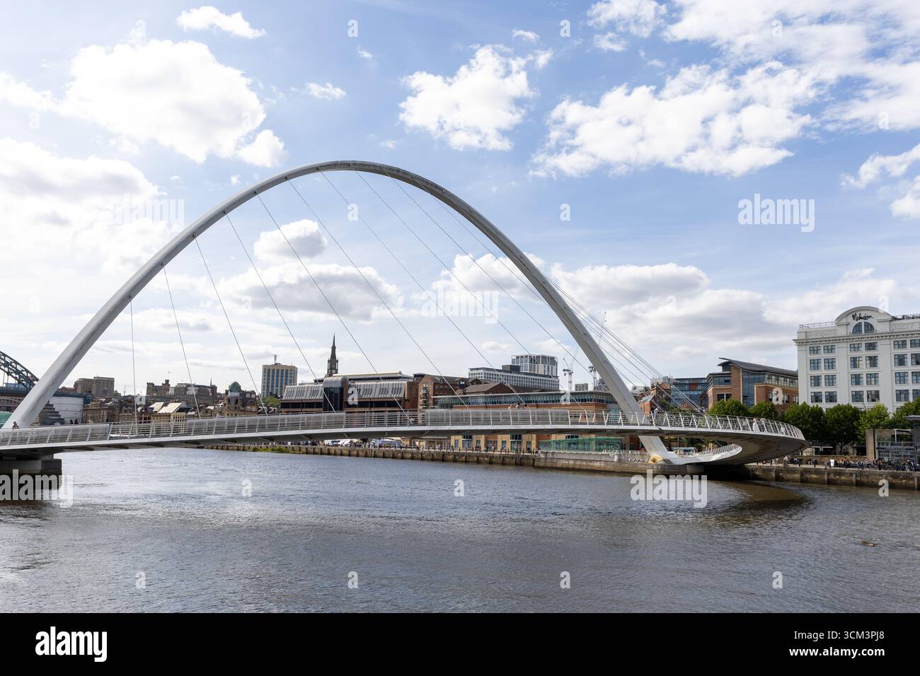 A modern bridge with a curved arch spans a river in front of a city ...