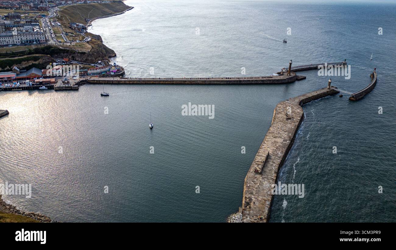 An aerial view of a harbor with stone piers, lighthouses, boats, and a ...