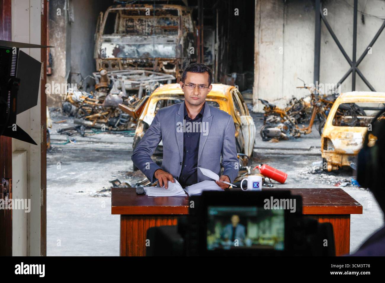 A news anchor reports live in front of the burnt and destroyed buildings and vehicles of ...