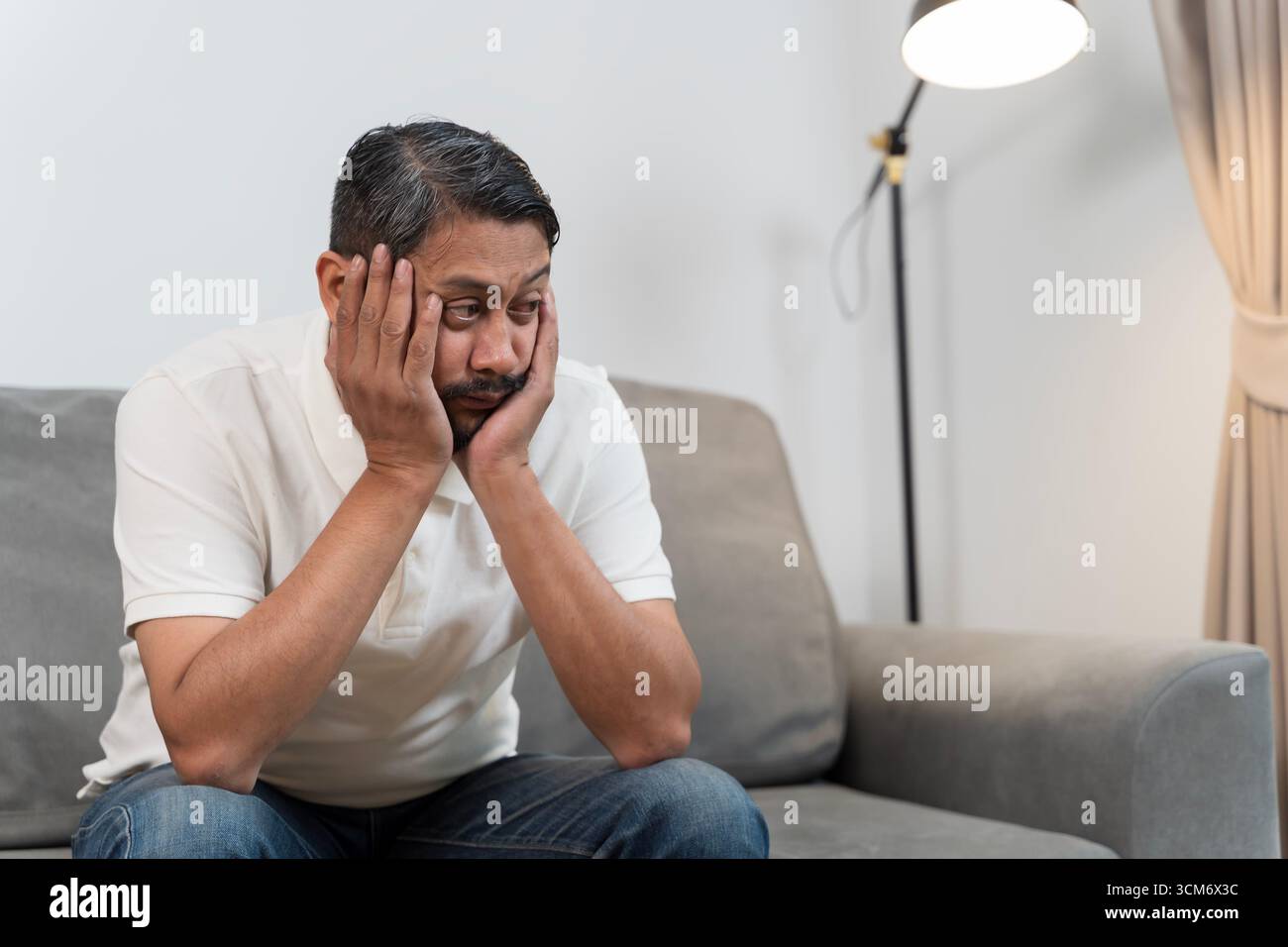 Portrait of depressed man sitting indoors with hands on face showing ...