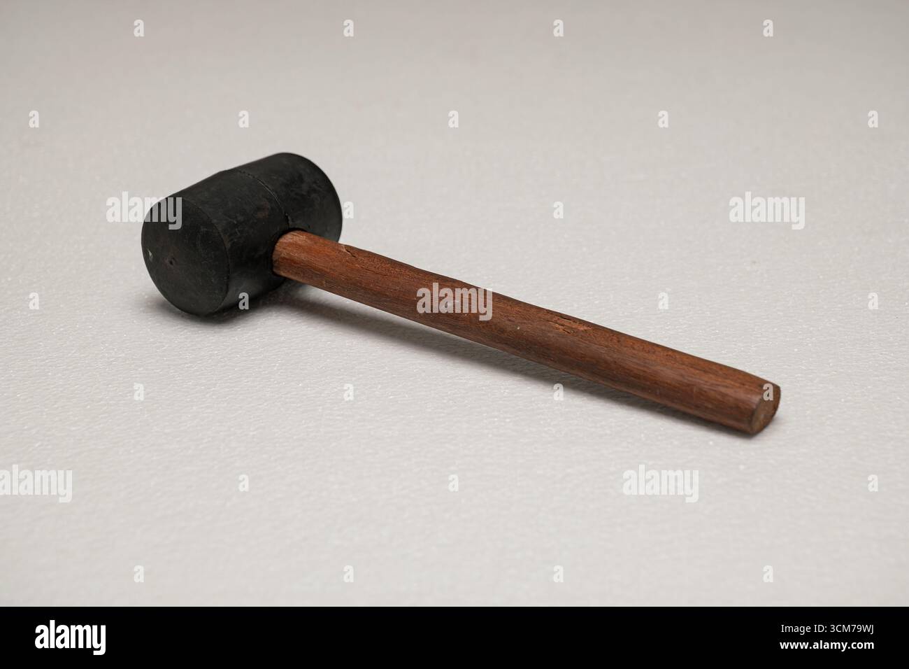 A wooden mallet with a black rubber head, resting on a light surface ...