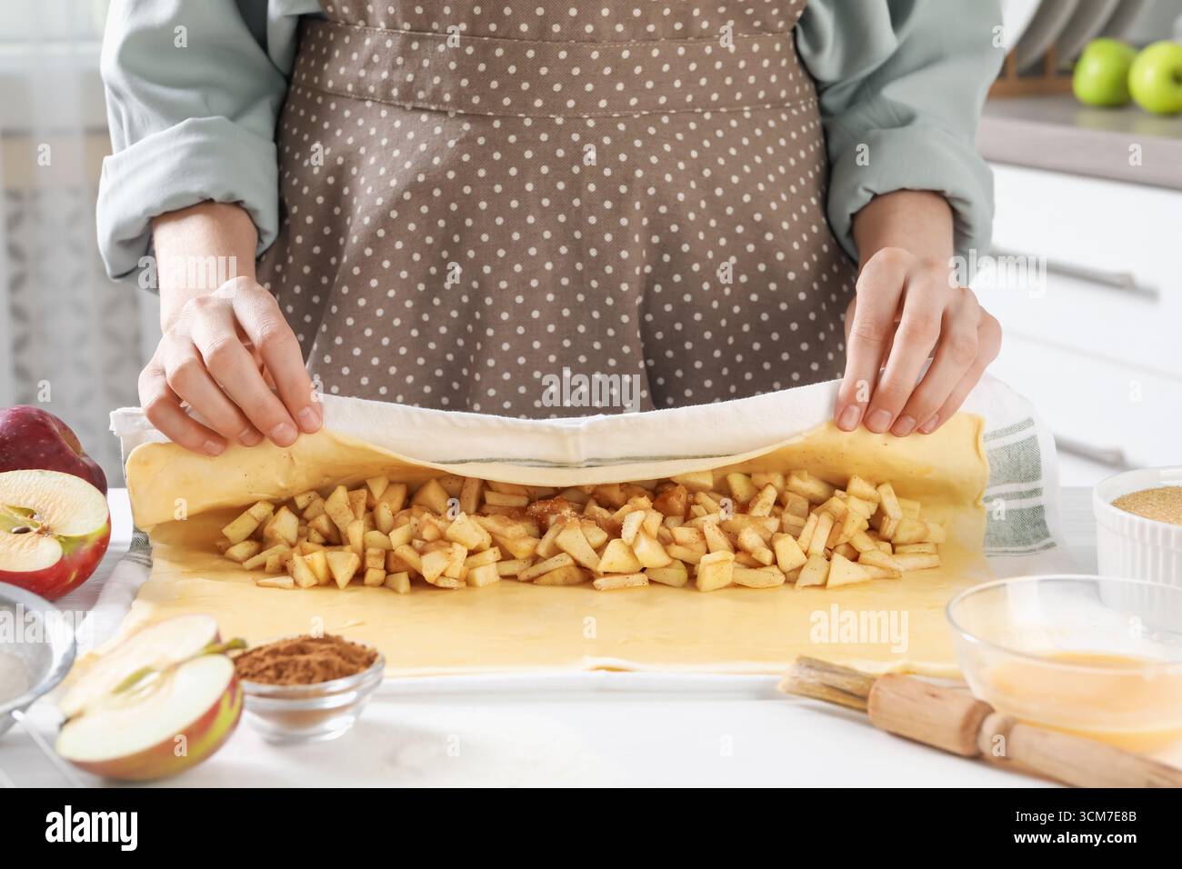 Woman making delicious apple strudel at white table in kitchen, closeup ...