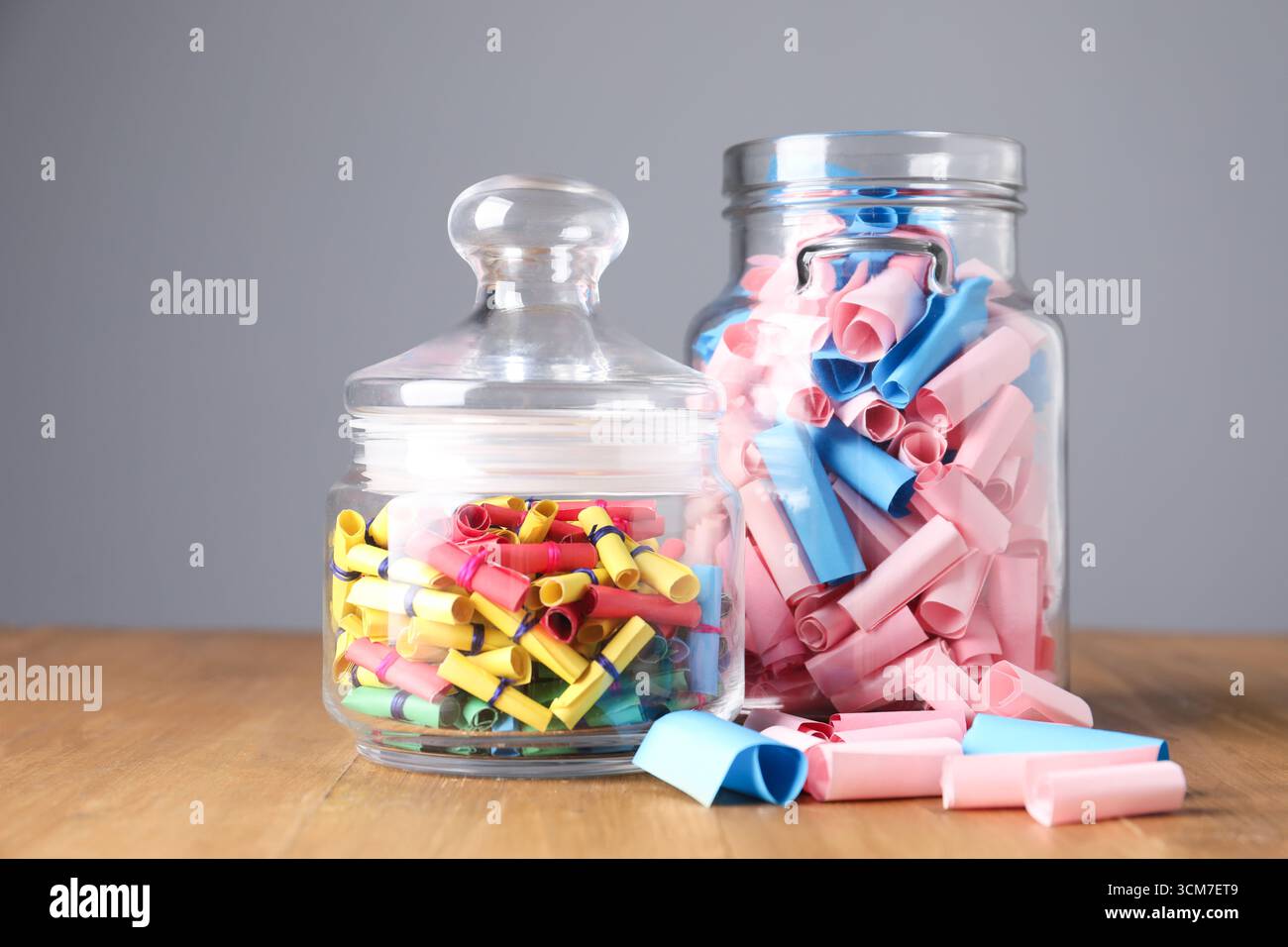 Colorful paper notes in glass jars on wooden table against grey ...