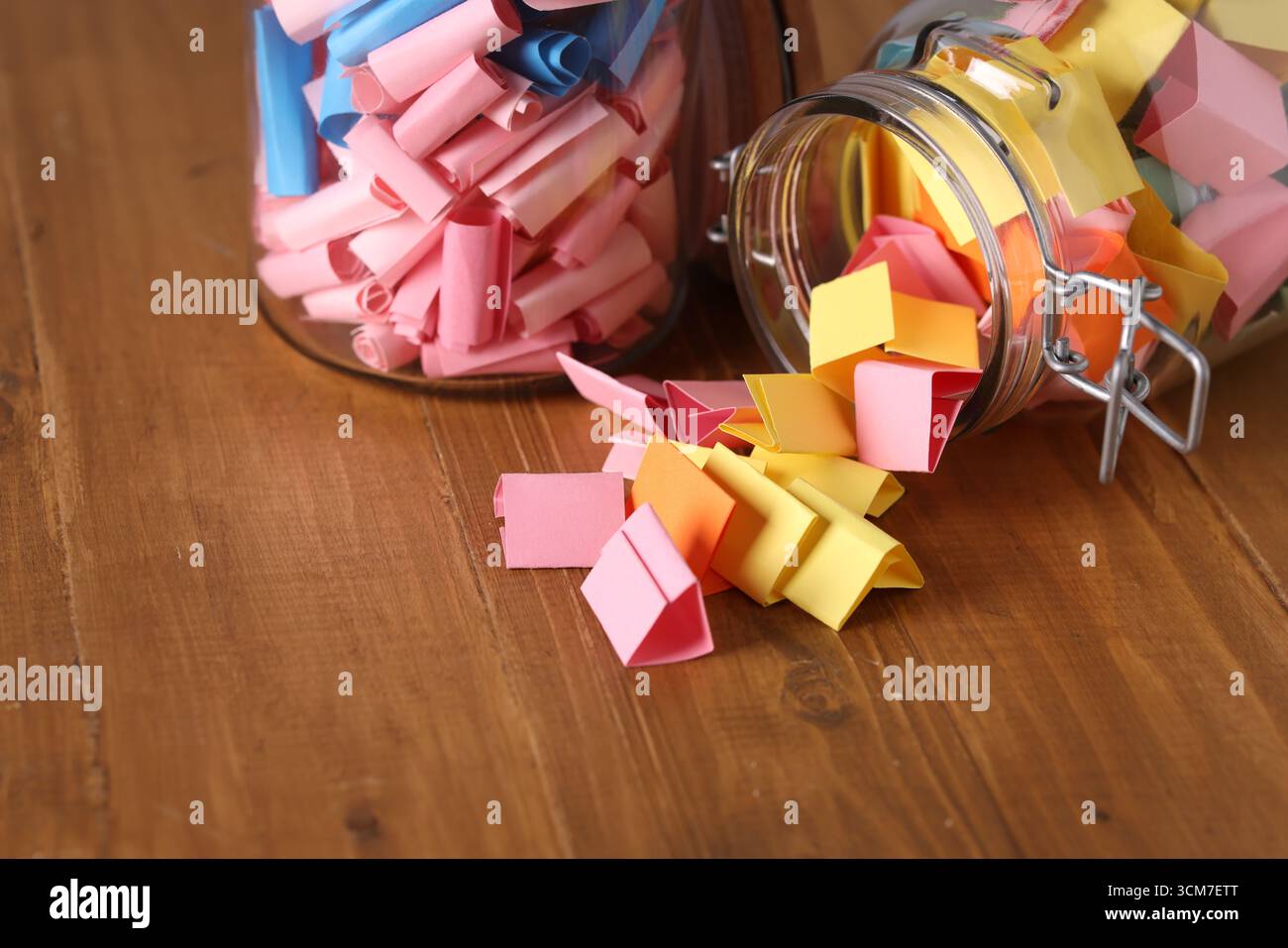 Colorful paper notes in glass jars on wooden table, closeup. Space for ...