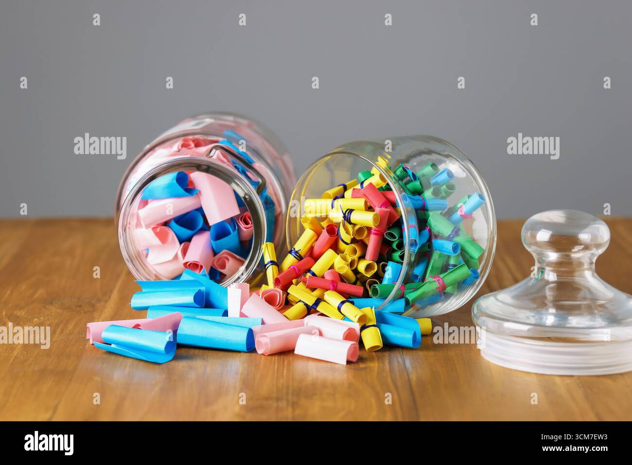 Colorful paper notes in glass jars on wooden table against grey ...