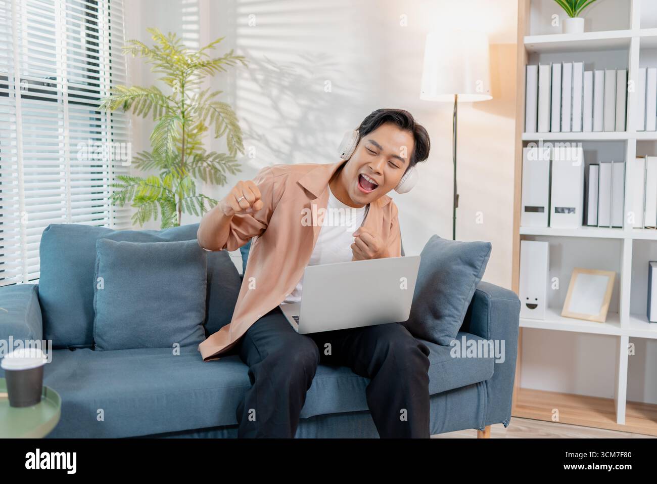 A cheerful young man sitting on a sofa singing with passion while ...
