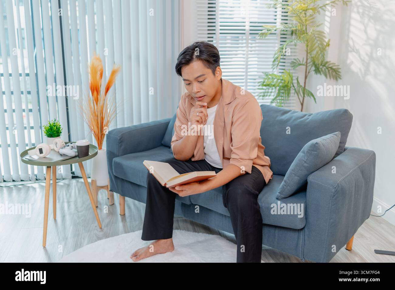 A young man sits comfortably on a sofa reading a book, appearing ...