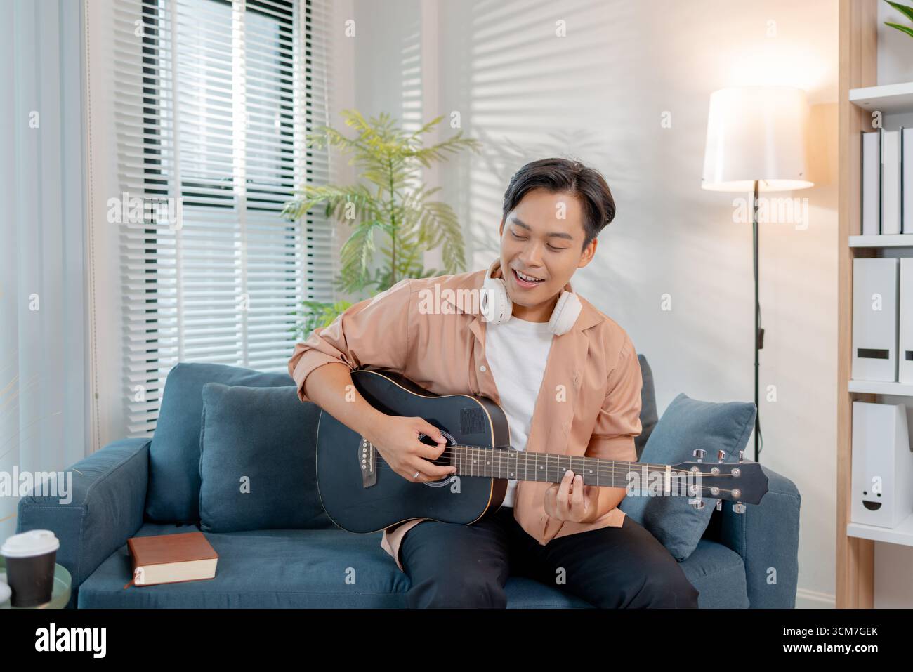 A young man is joyfully playing guitar in his living room, enjoying the ...