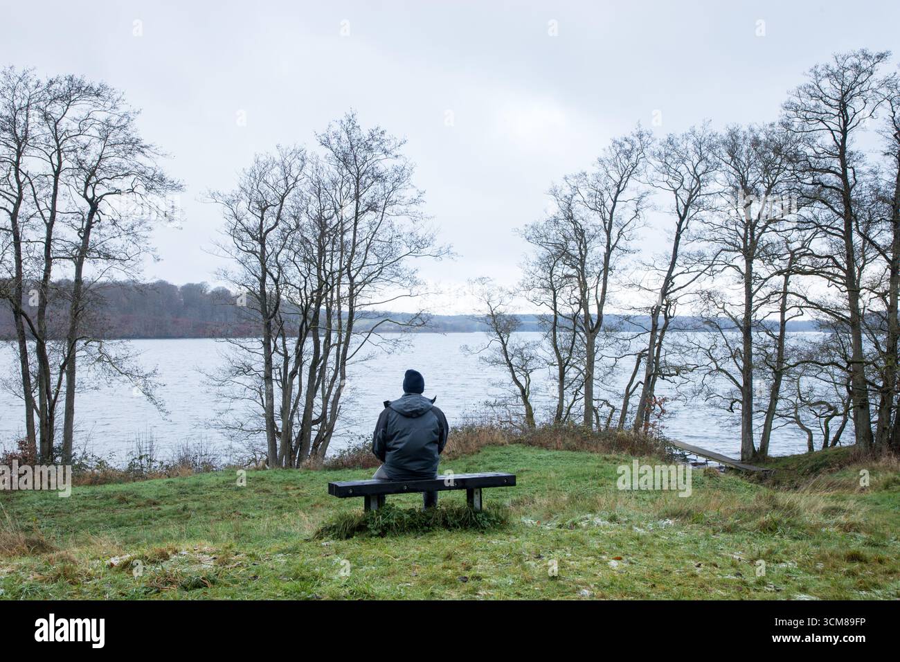 alone man sitting on bench looking out over lake at autumn a grey day ...