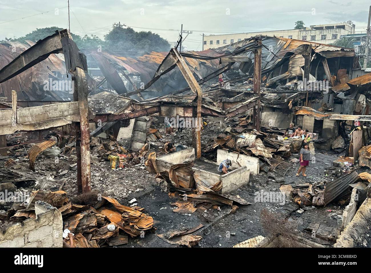 Residents stand beside the remains of a building after a fire gutted ...